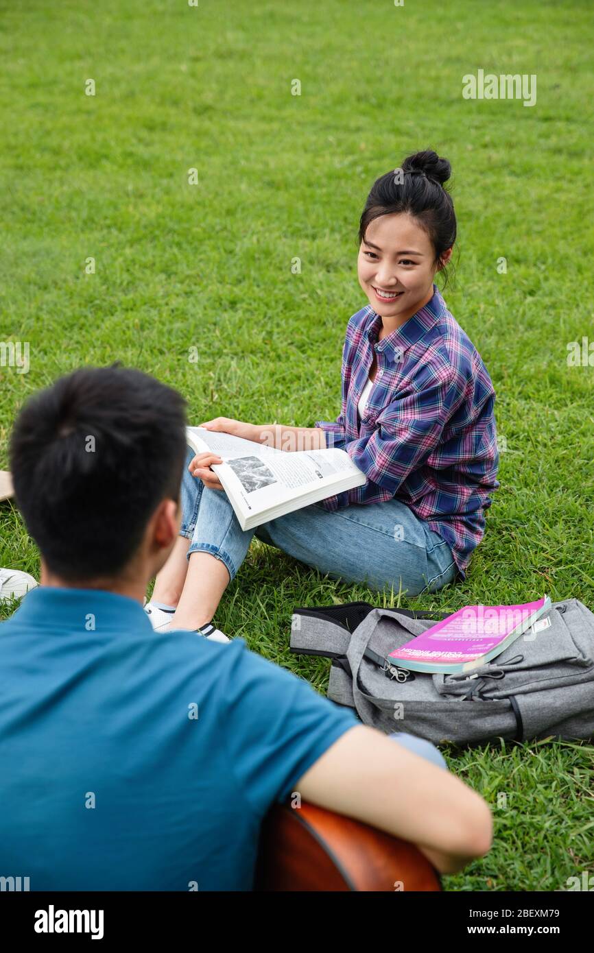 Happy girl sitting on the grass to listen to the classmate to play ...