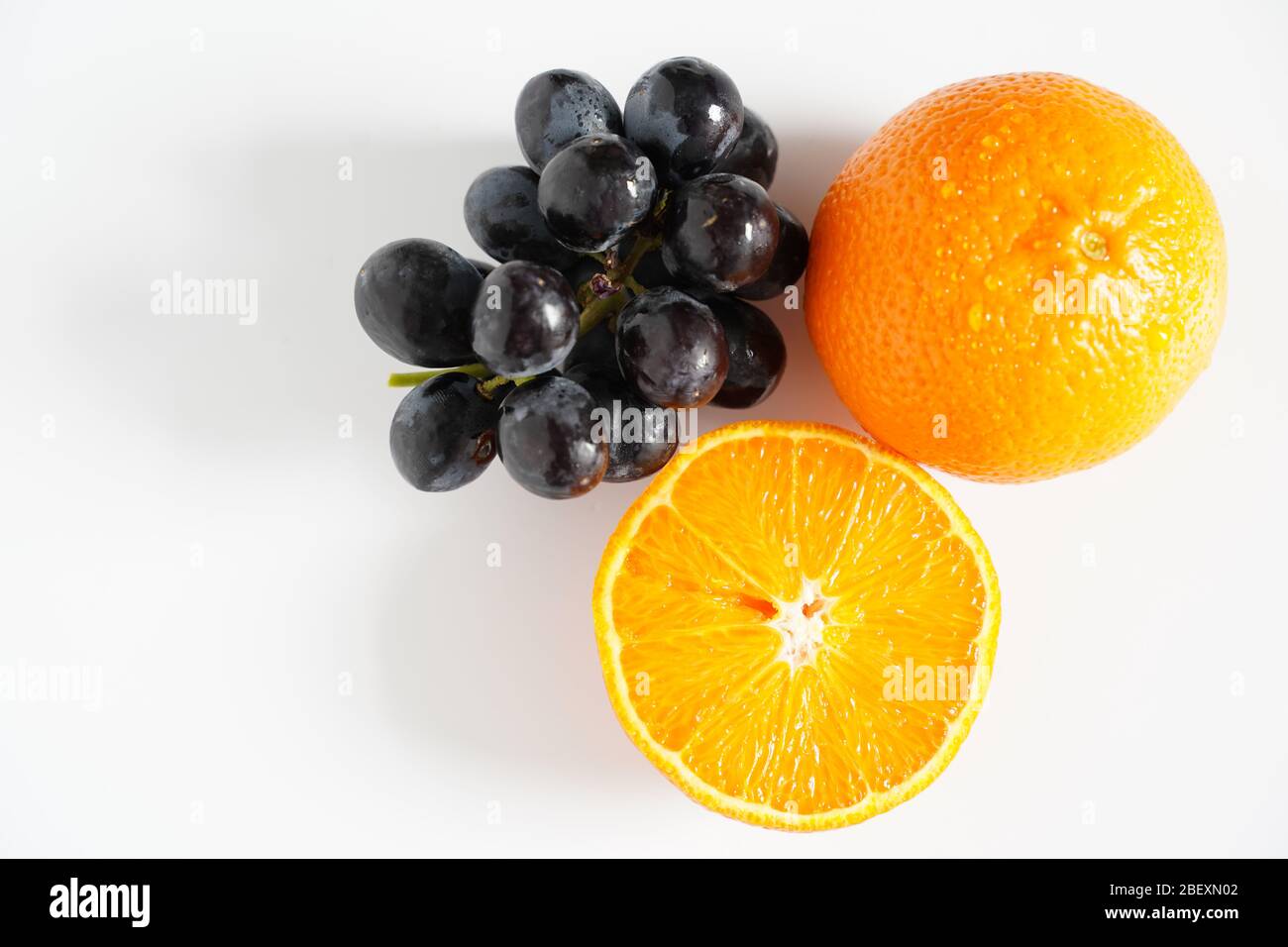 A sliced orange and a bunch of black grapes against a plain white ...