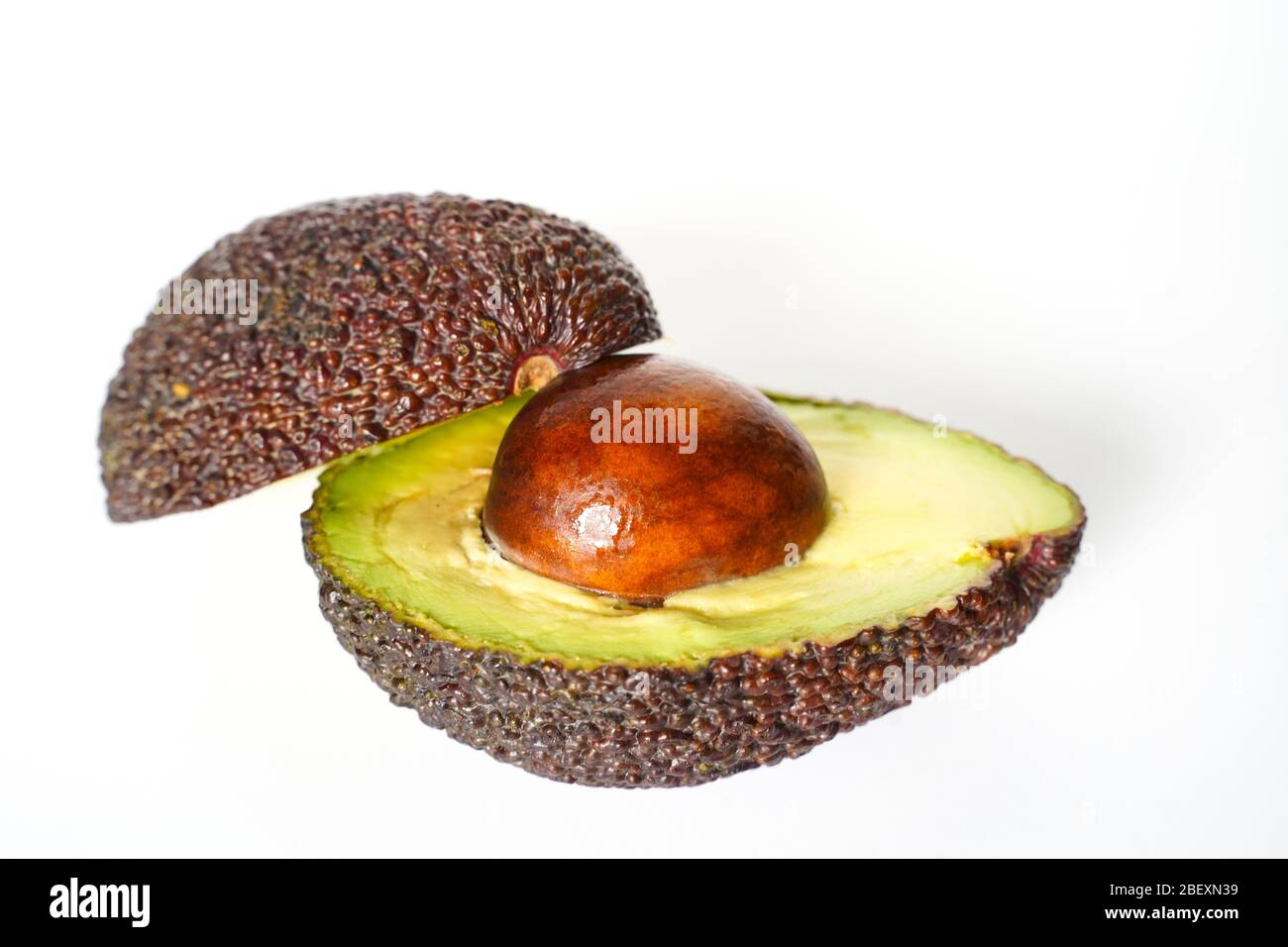 An avocado sliced in half to reveal the core against a plain white ...