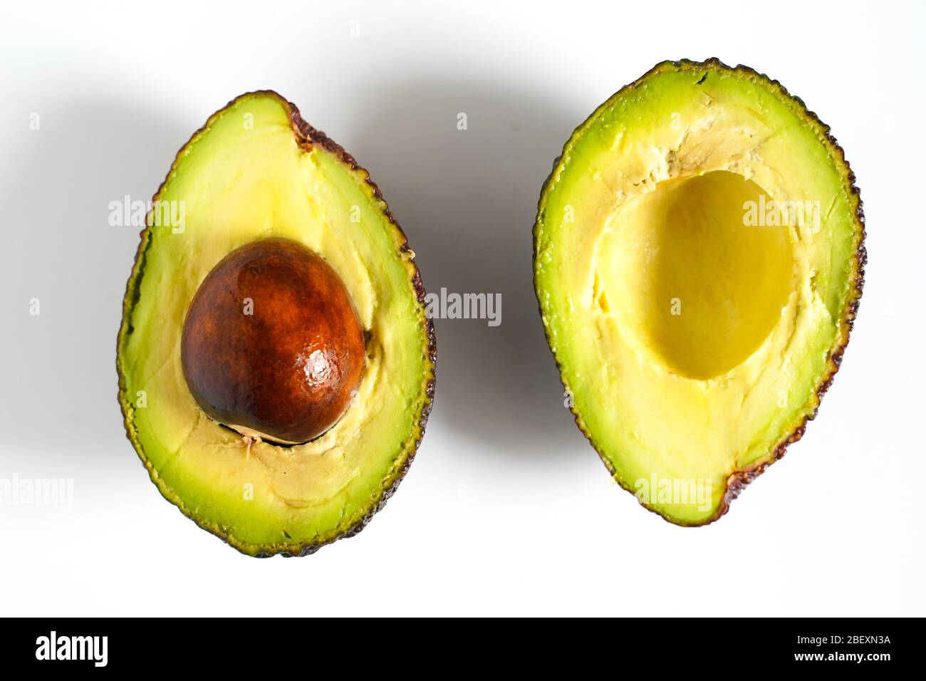 An avocado sliced in half to reveal the core against a plain white ...