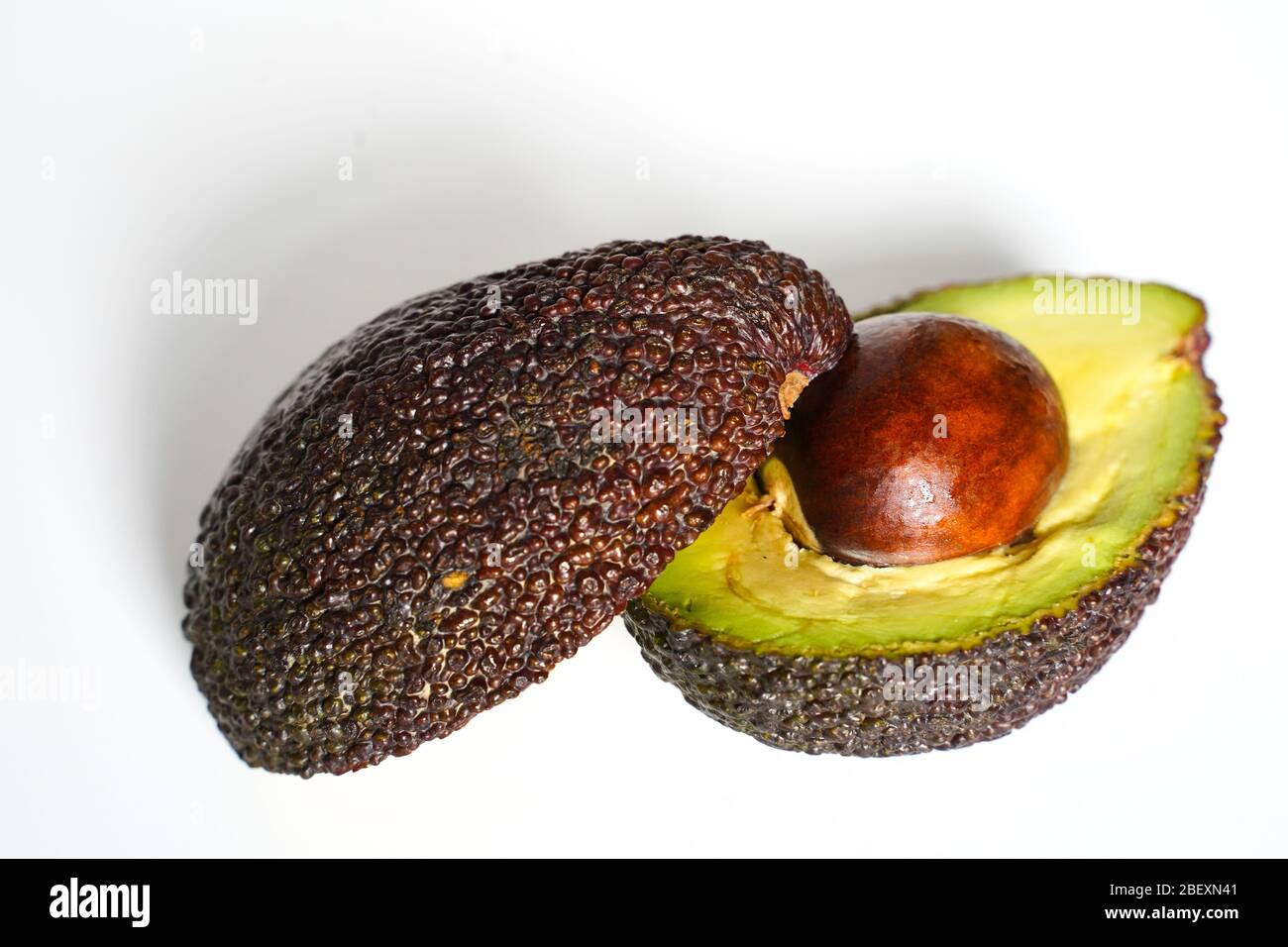 An avocado sliced in half to reveal the core against a plain white ...