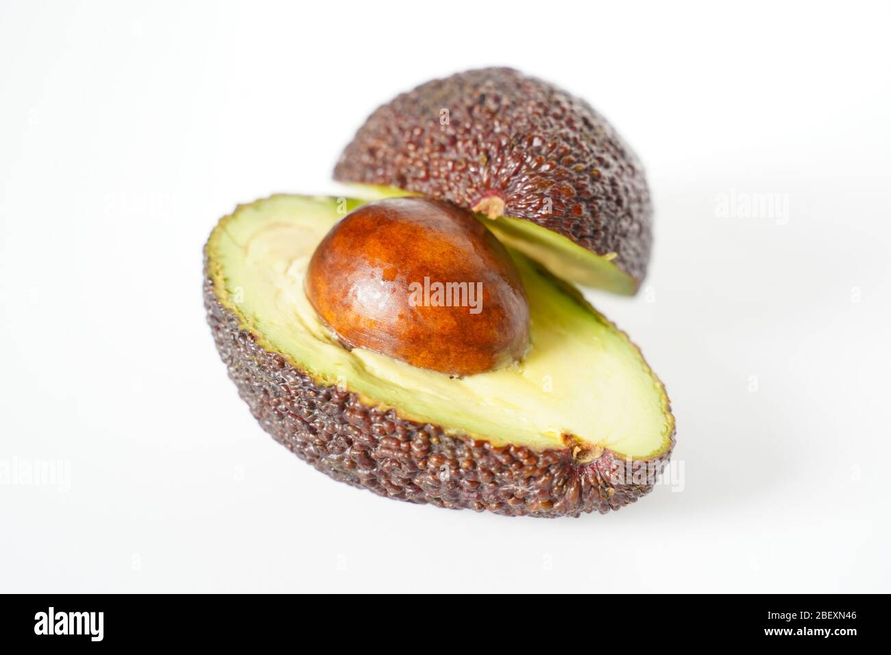An avocado sliced in half to reveal the core against a plain white ...