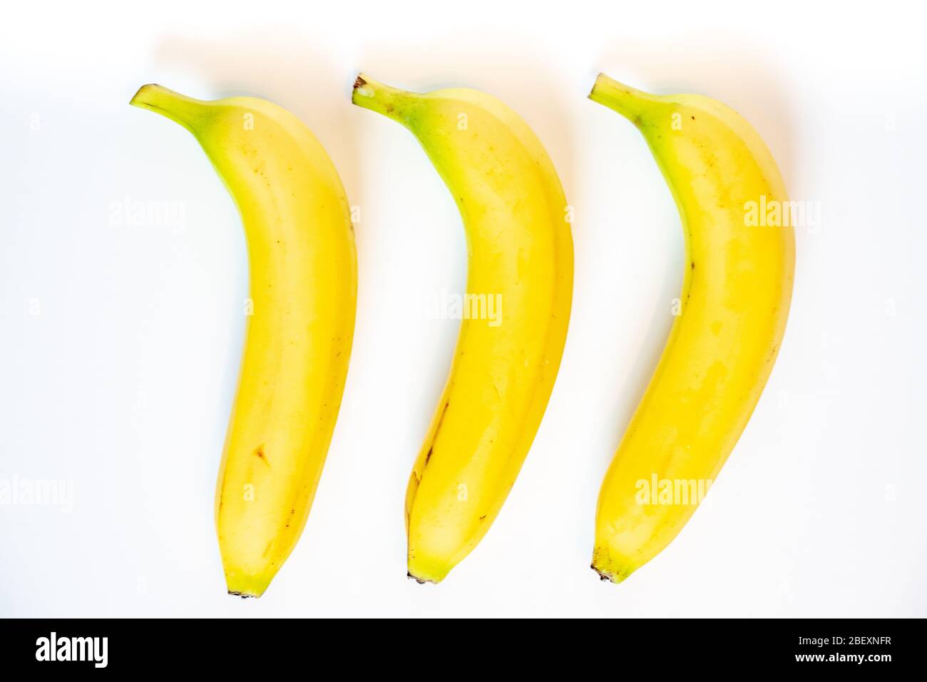 Three whole bananas laid side by side against a plain white background ...