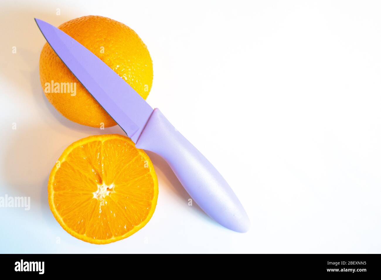 Two halves of orange with a sharp knife on a plain white background ...
