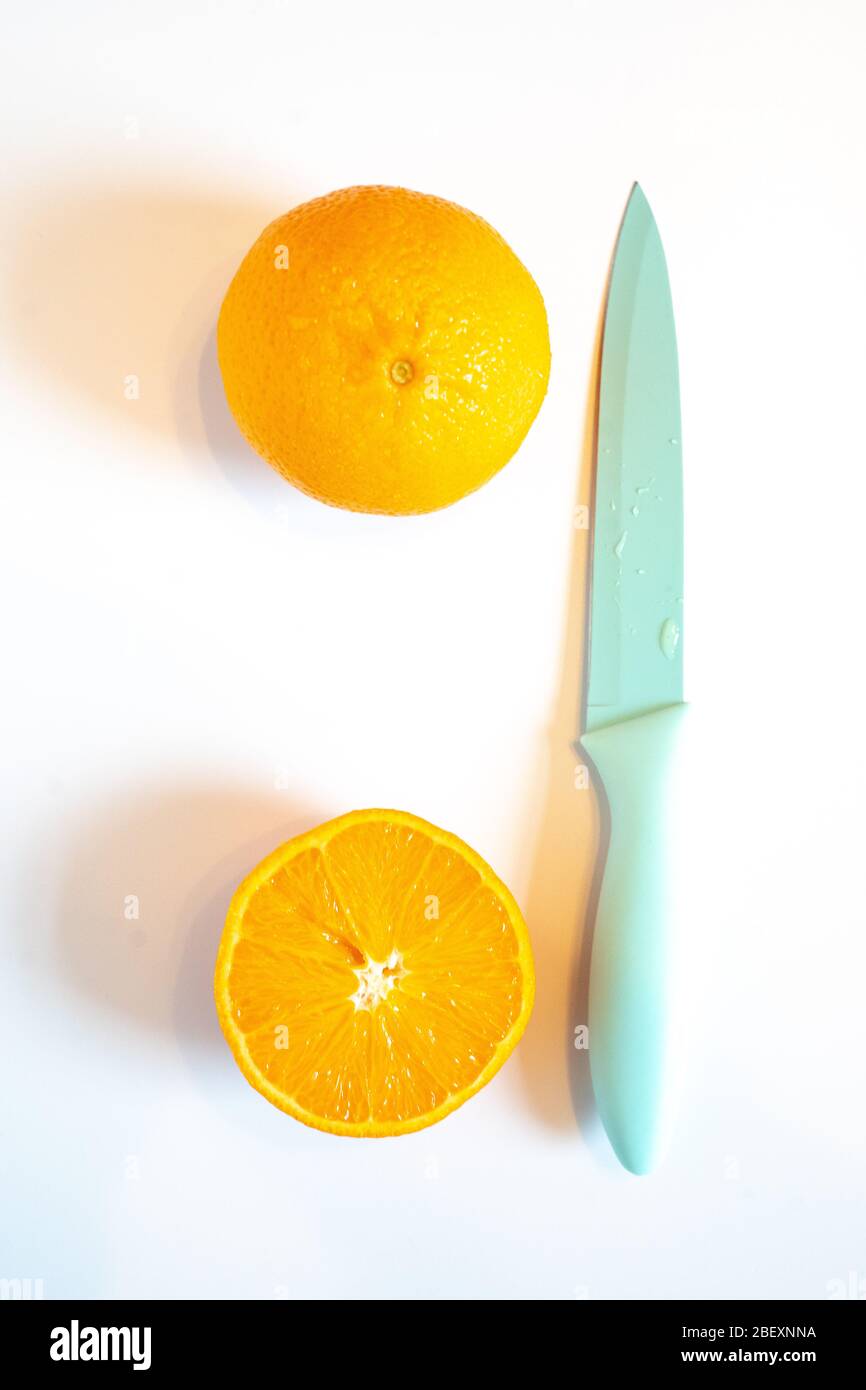 Two halves of orange with a sharp knife on a plain white background ...