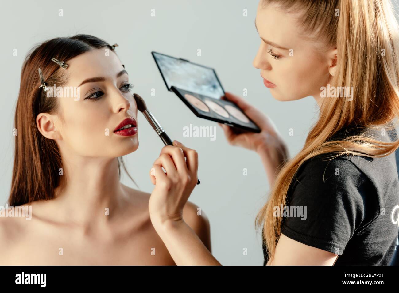 beautiful makeup artist applying concealer on attractive model isolated ...