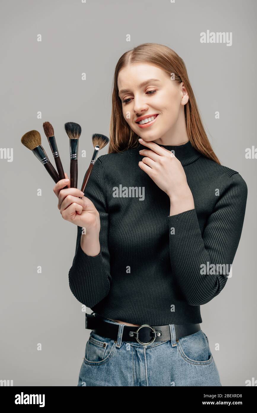 happy makeup artist holding cosmetic brushes isolated on grey Stock ...
