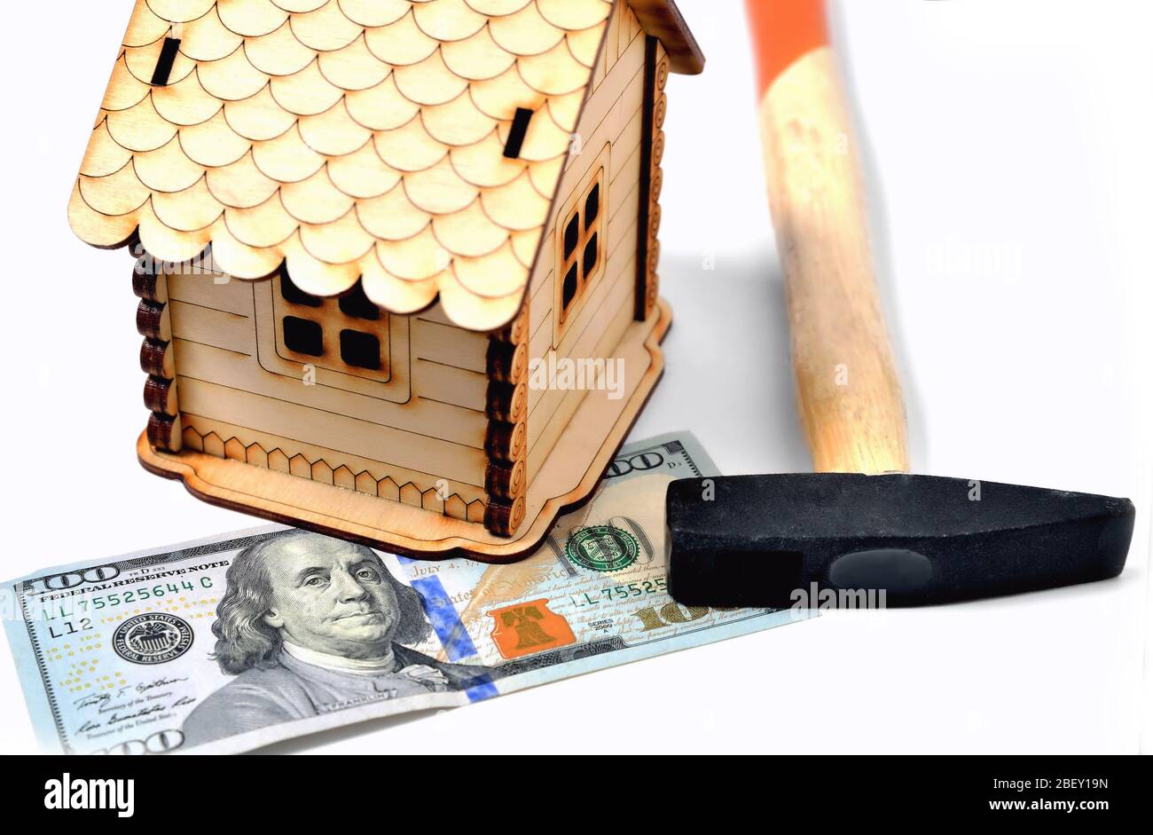 Wooden toy house, a banknote of 100 dollars and a hammer on a white ...