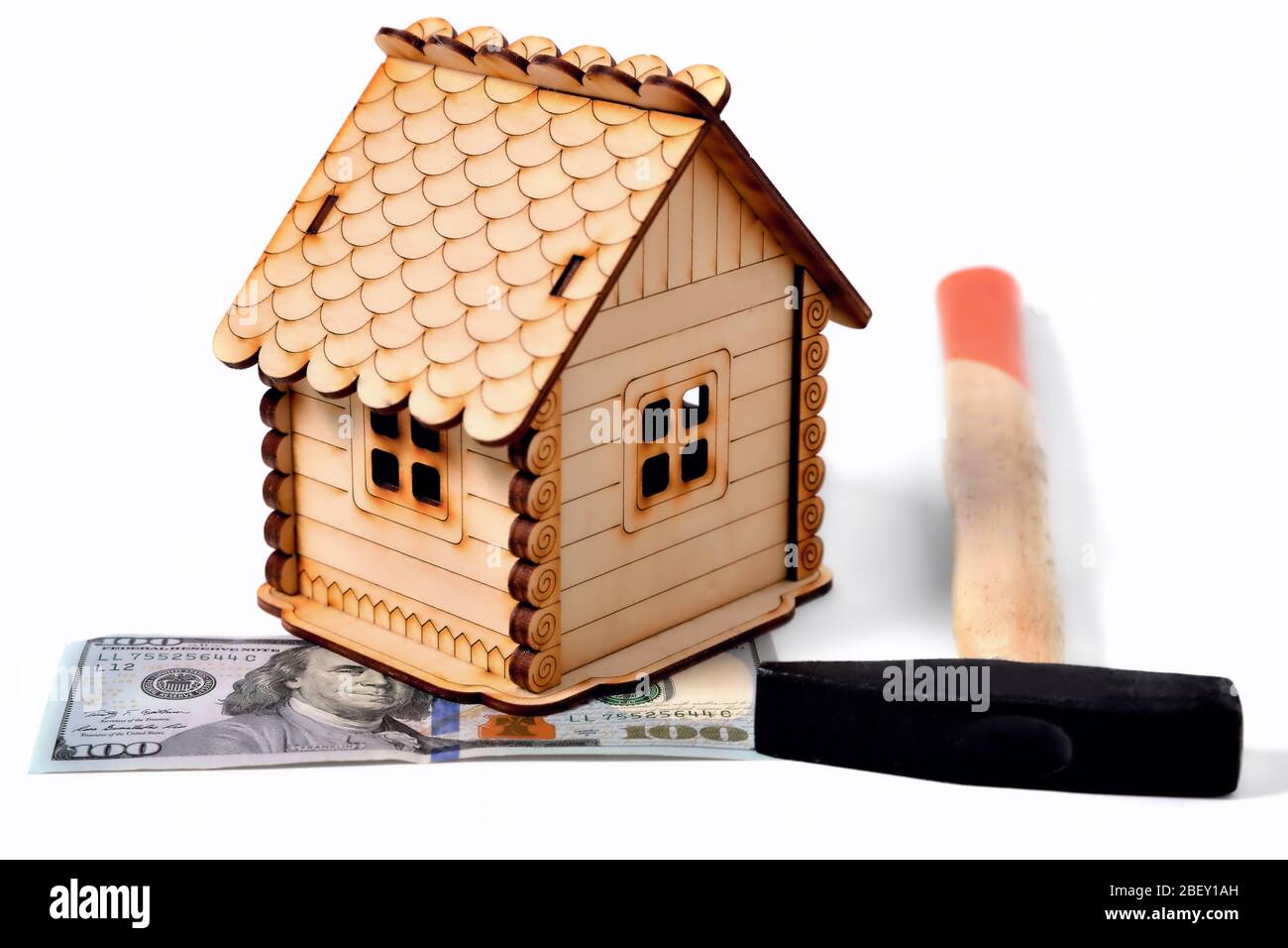 Wooden toy house, a banknote of 100 dollars and a hammer on a white ...