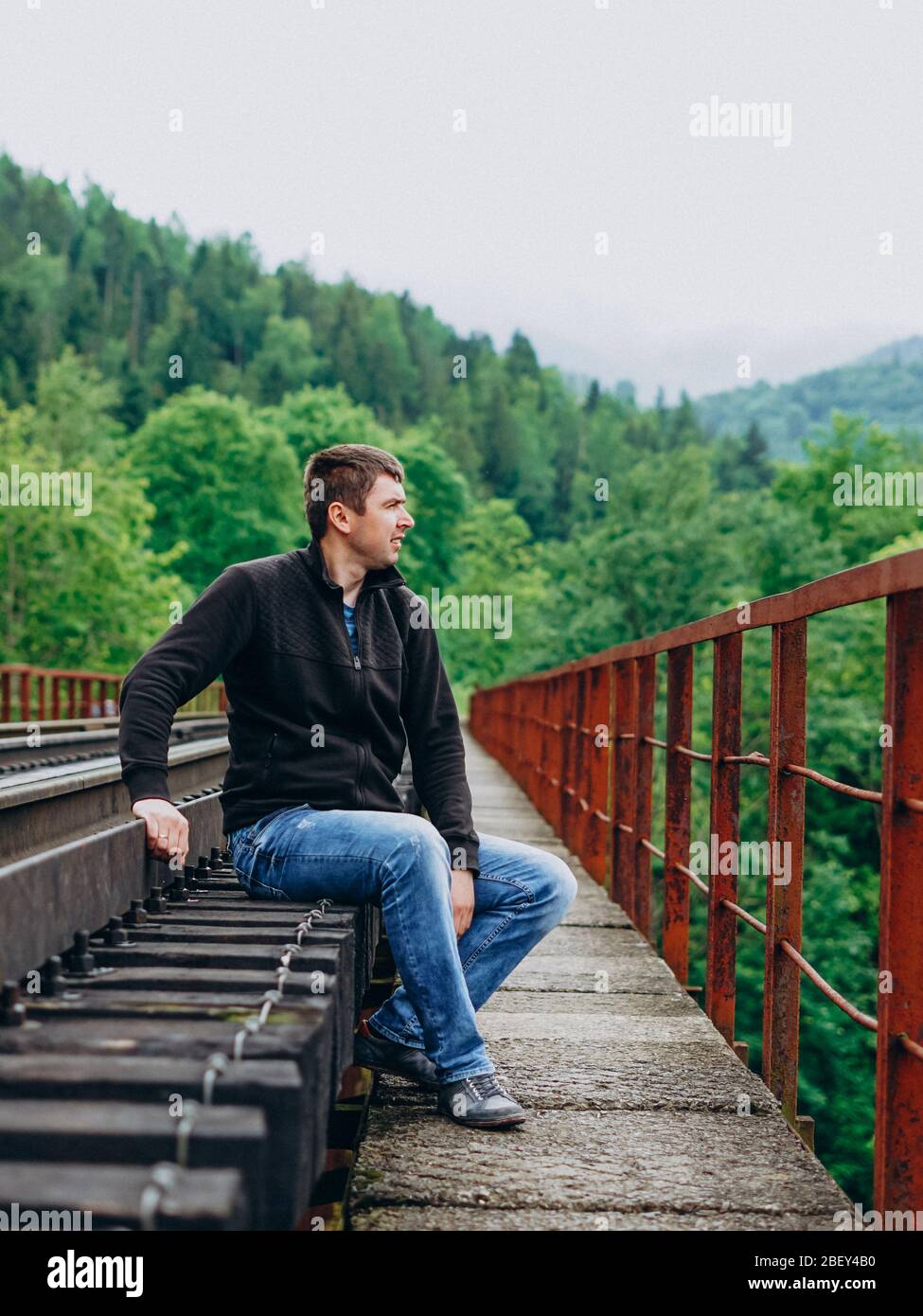 A man in jeans sits on a railway track. Railroad track on forest ...