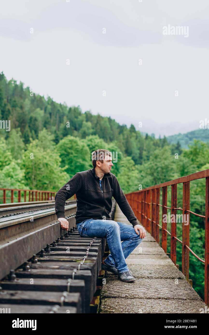 A man in jeans sits on a railway track. Railroad track on forest ...