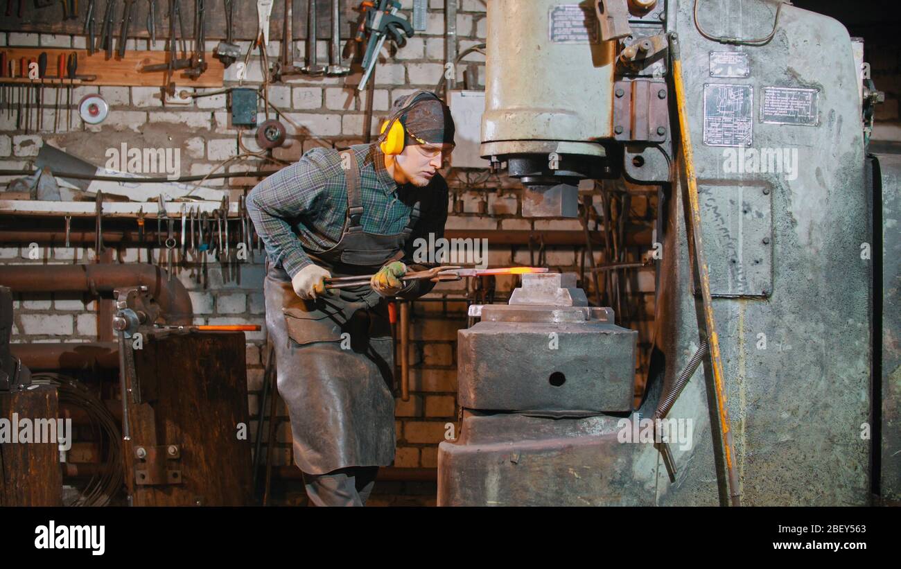 Forging industry - a man blacksmith putting the hot piece of metal ...