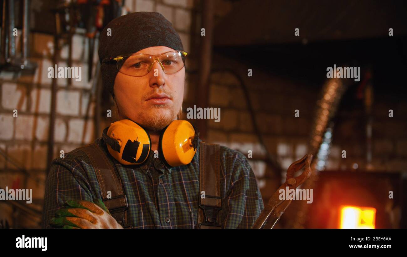 Forging industry - a man blacksmith holding forceps and looking in the ...