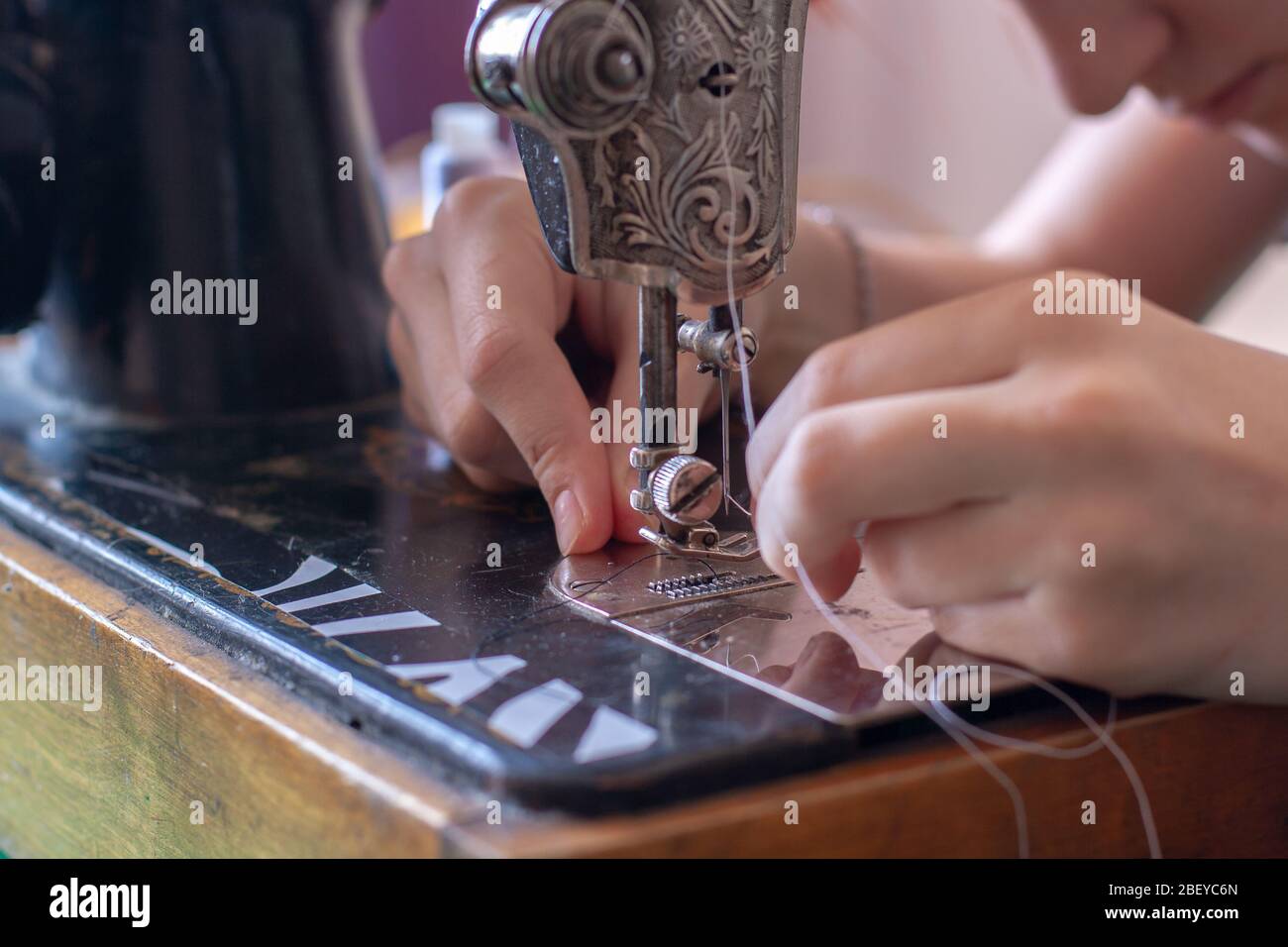 A seamstress inserts a thread into a needle eye on an old retro sewing ...