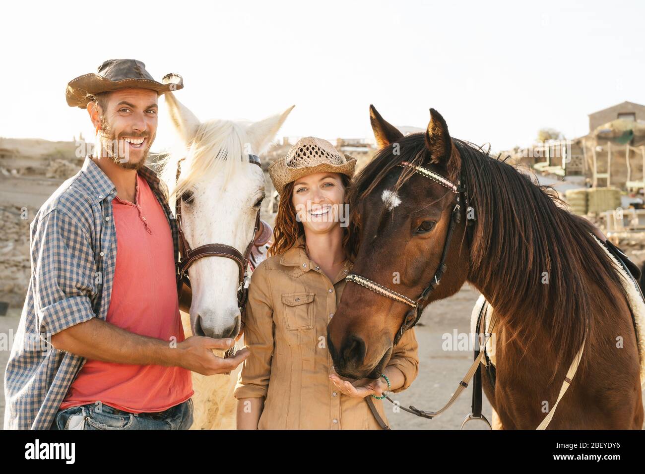 Happy couple having fun with horses inside stable - Young farmers ...