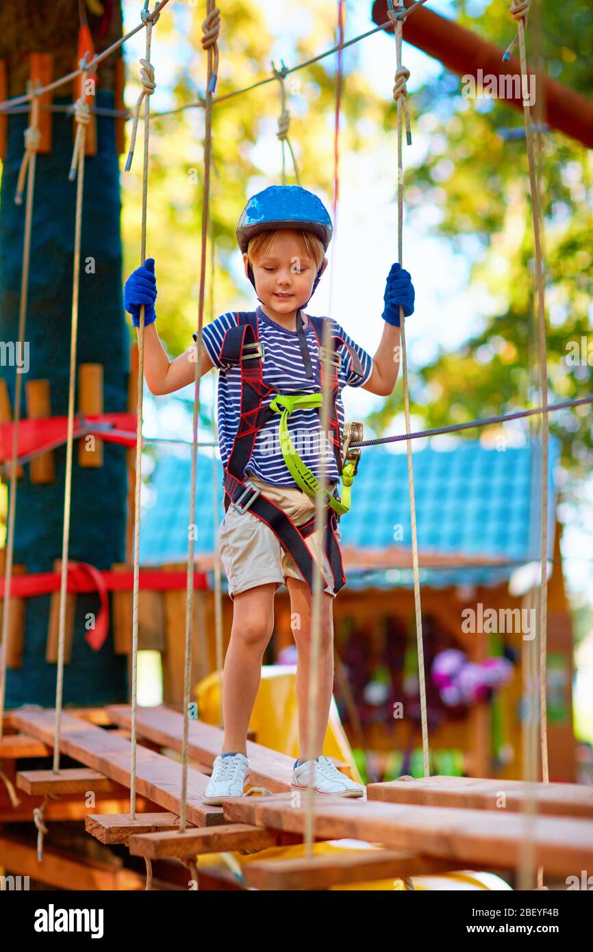 young boy passing the cable route high among trees, extreme sport in ...