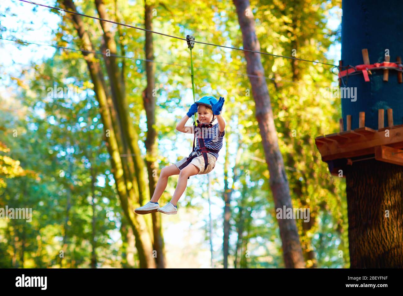 young boy passing the cable route high among trees, extreme sport in ...