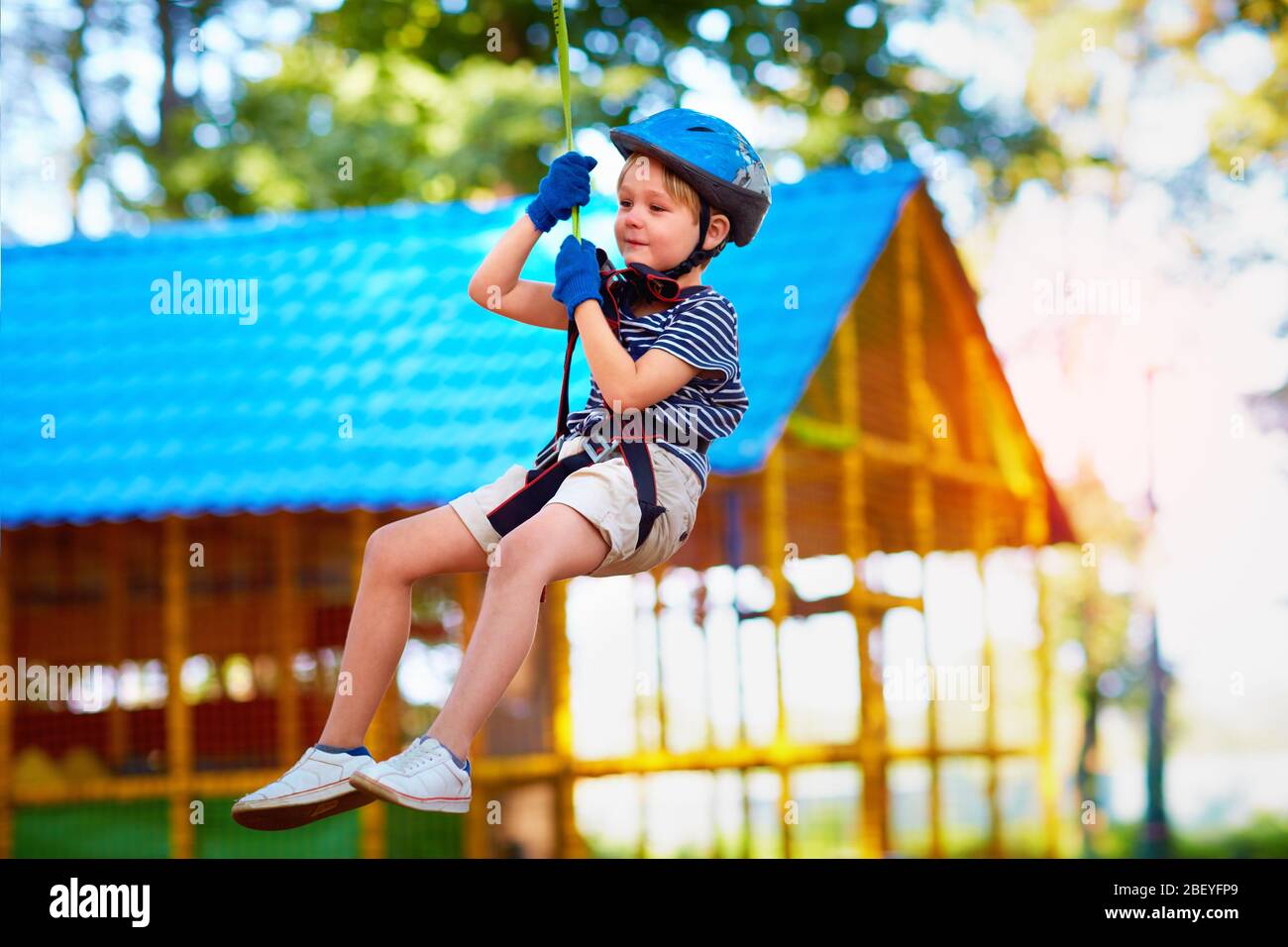 young boy passing the cable route high among the trees, extreme sport ...