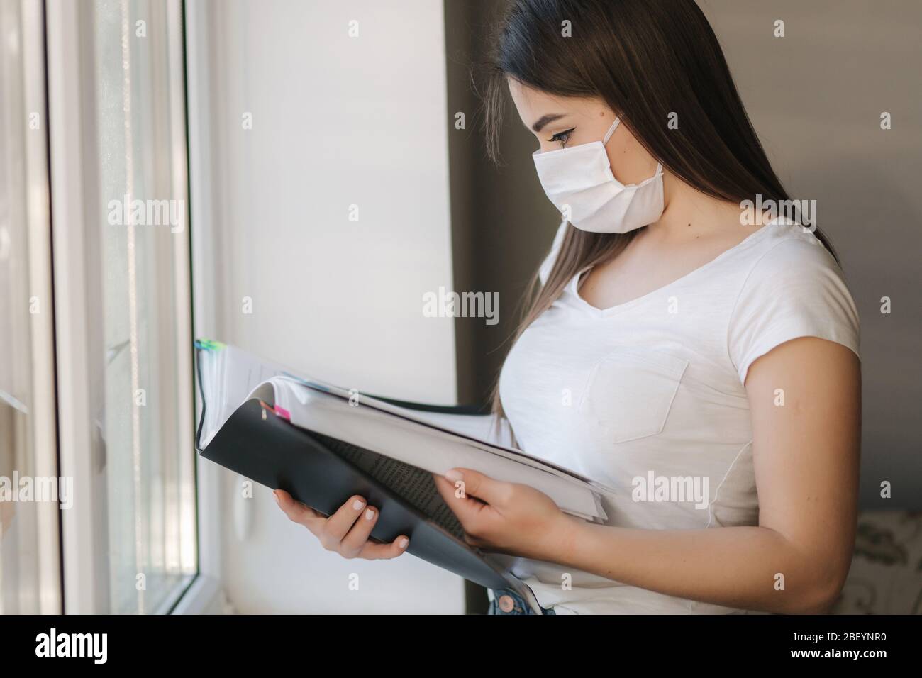 Female doctor in white t-shirt and white mask reviewing documentation Stock Photo - Alamy