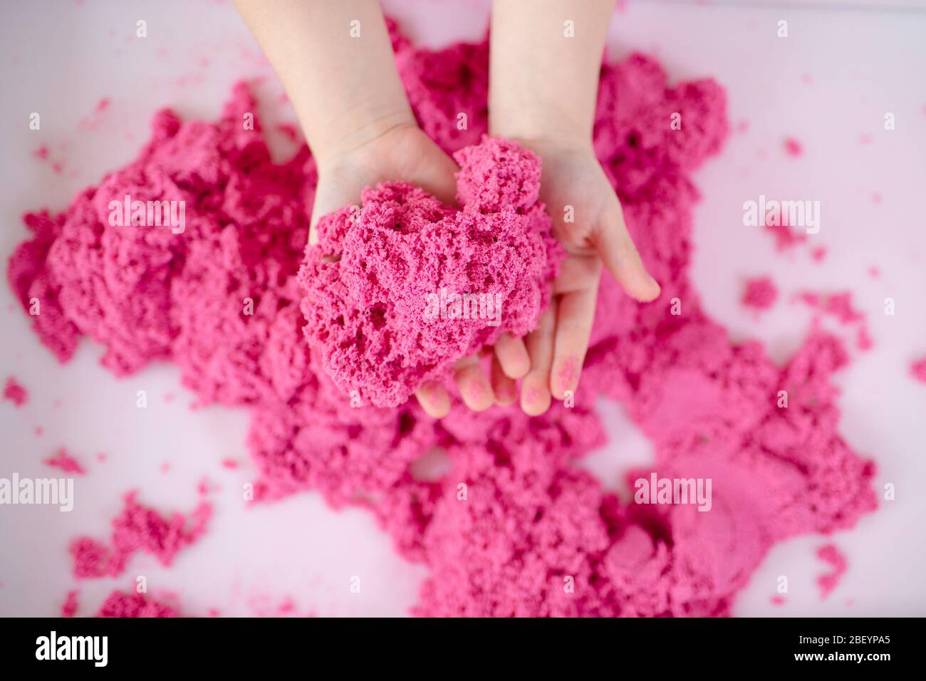 Pink magic sand in a kids hands on a white background close up. Early ...