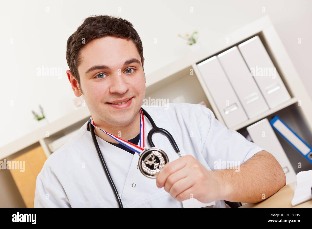 Proud doctor at the desk shows a medal around his neck Stock Photo - Alamy