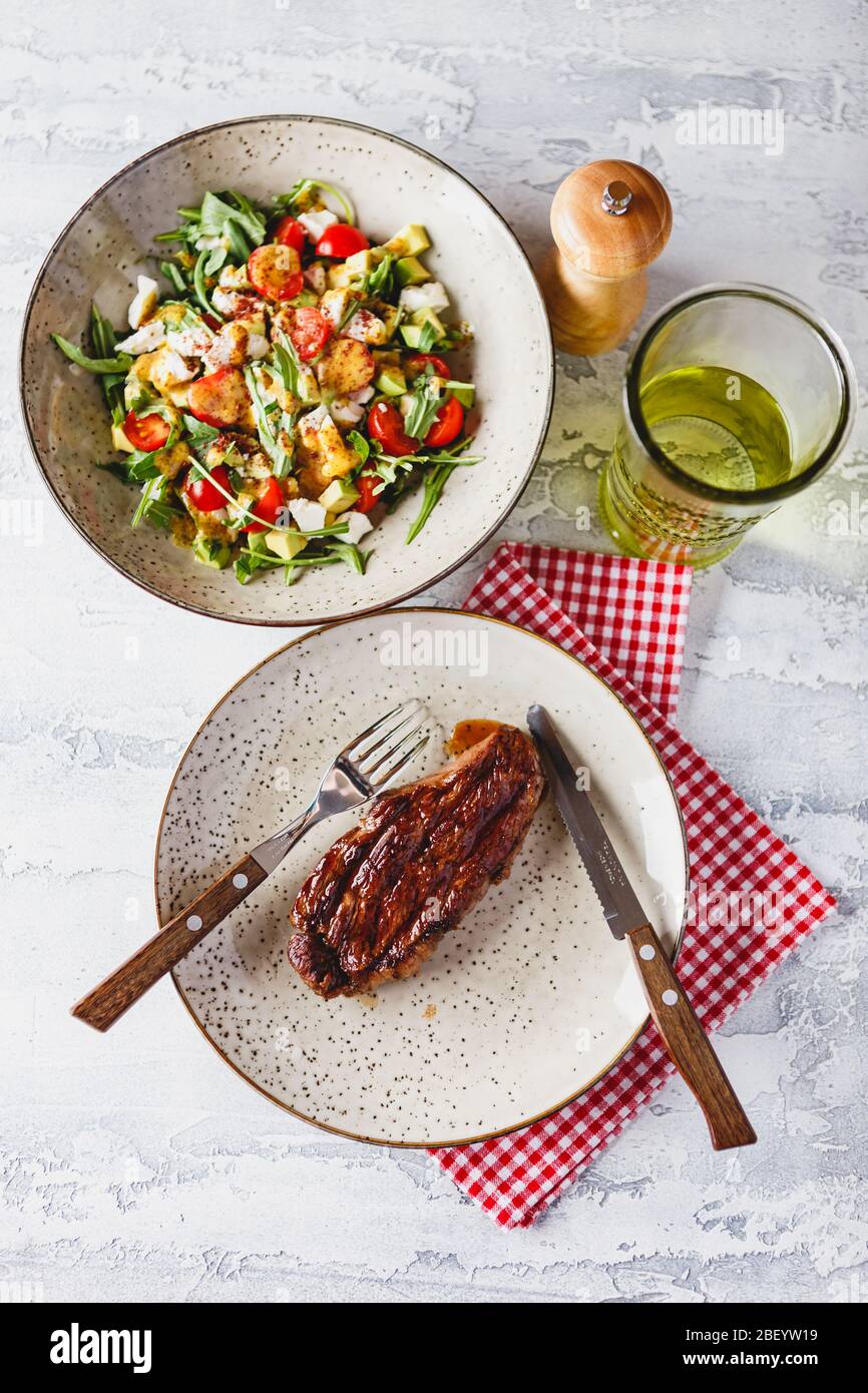 Grilled steaks and vegetable salad on light background. Table setting ...
