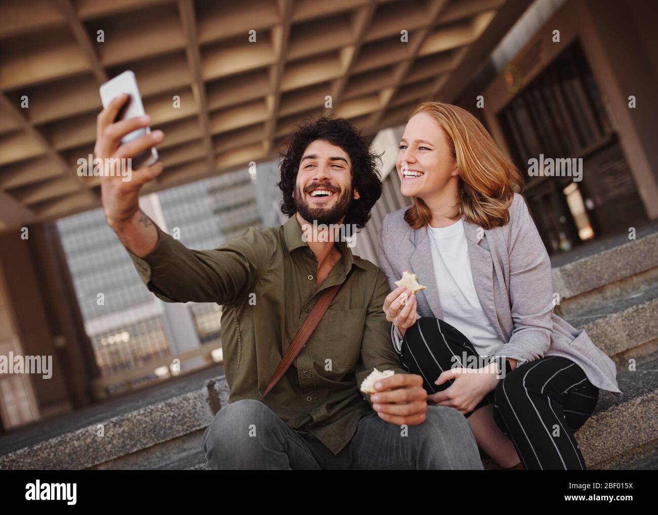 Happy professional couple taking selfie using smartphone while eating ...
