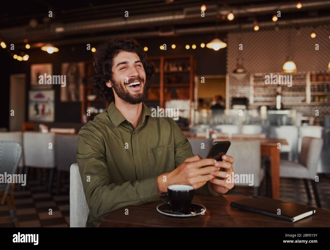 Portrait of handsome young man laughing while reading funny message on ...