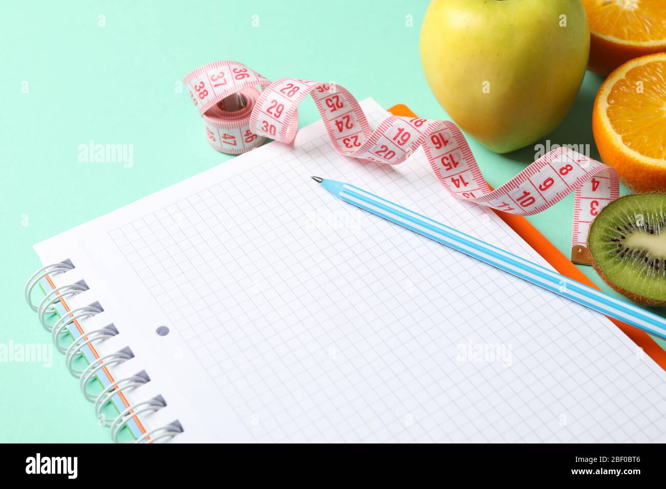Notebook, measuring tape, pen and vegetarian food on mint background ...