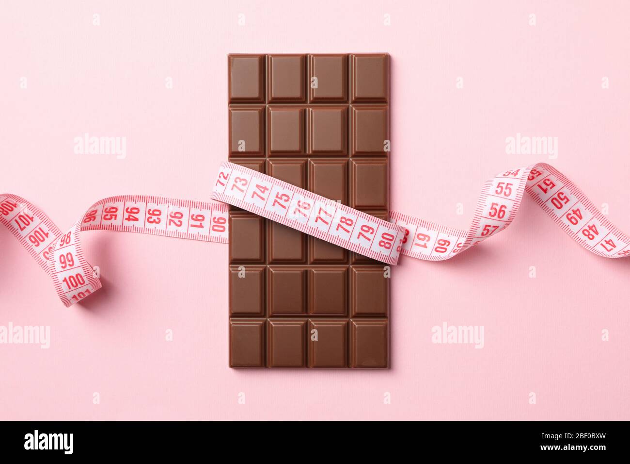 Measuring tape and chocolate bar on pink background Stock Photo - Alamy