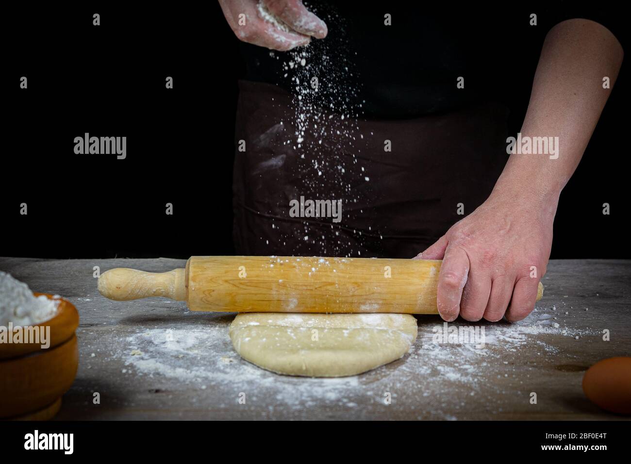 Man hands kneading bread dough on a wooden table with black background ...