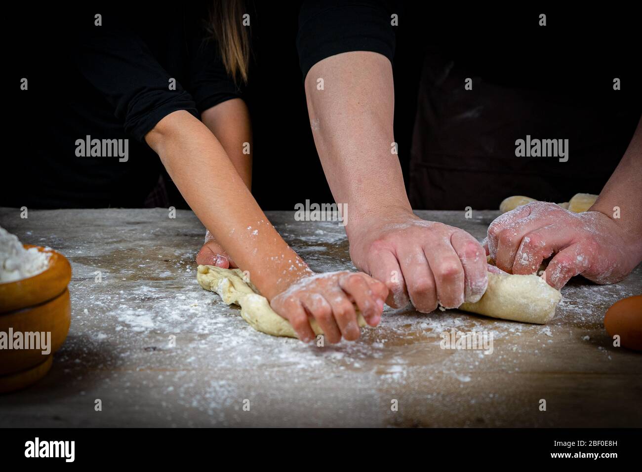 Hands of man and girl kneading bread dough on a wooden table with black ...