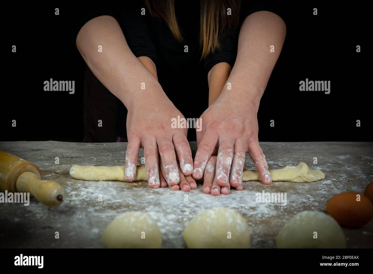Hands of man and girl kneading bread dough on a wooden table with black ...