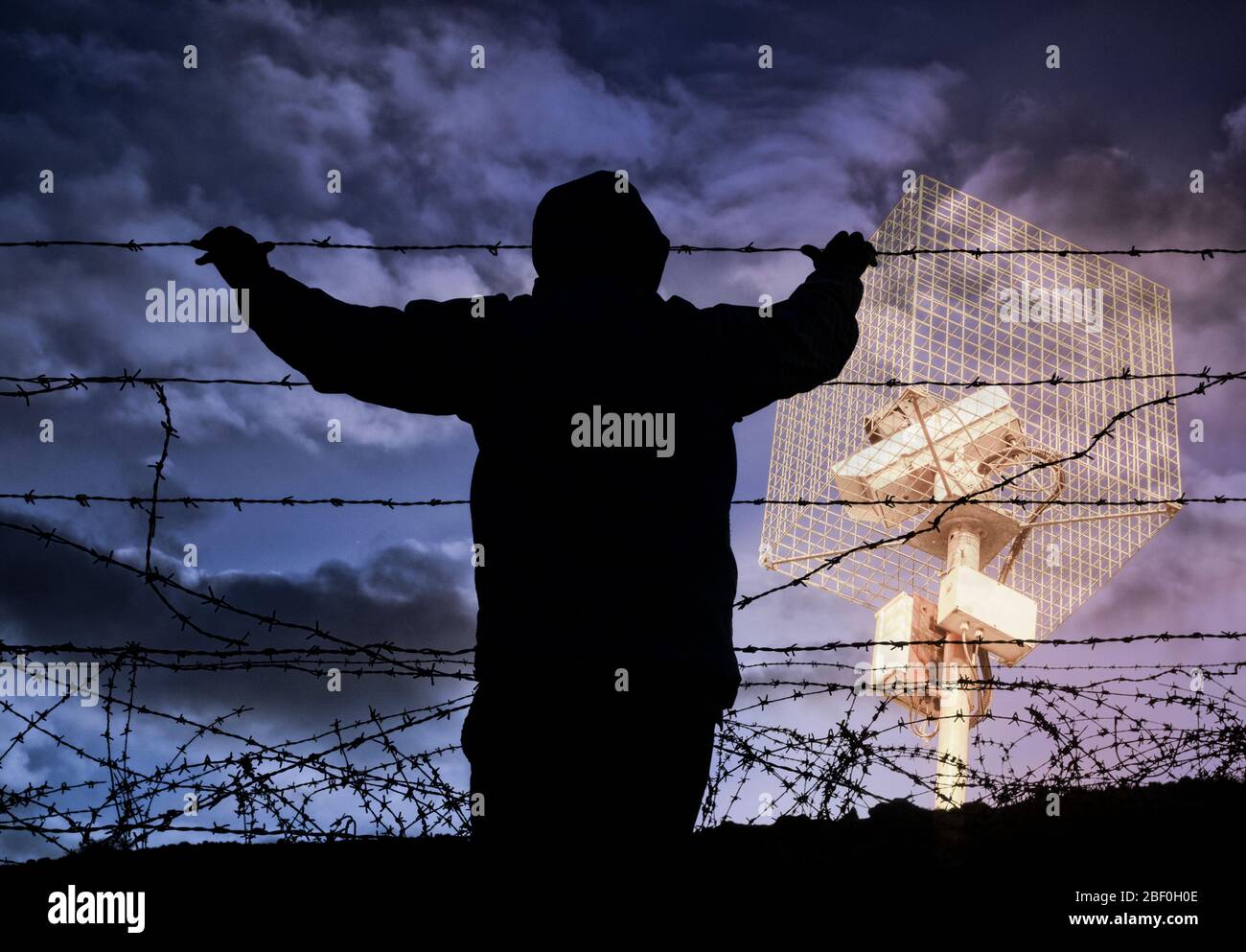 Rear view of man looking over barbed wire fence with CCTV security ...