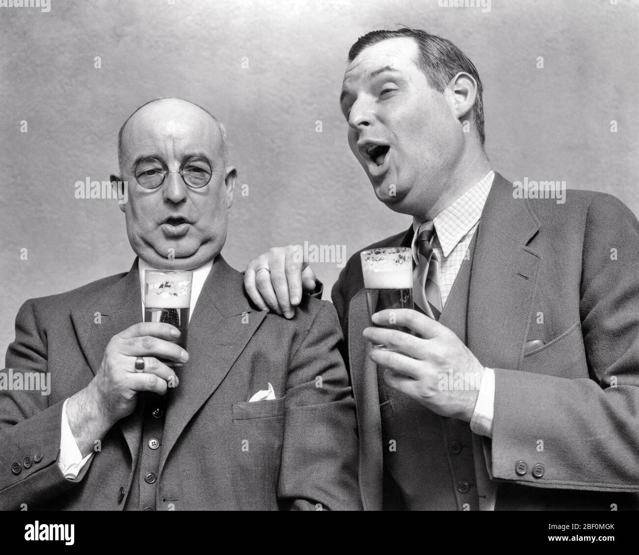 1930s TWO DRUNKEN BUSINESSMEN CELEBRATING SINGING AND DRINKING BEER ...