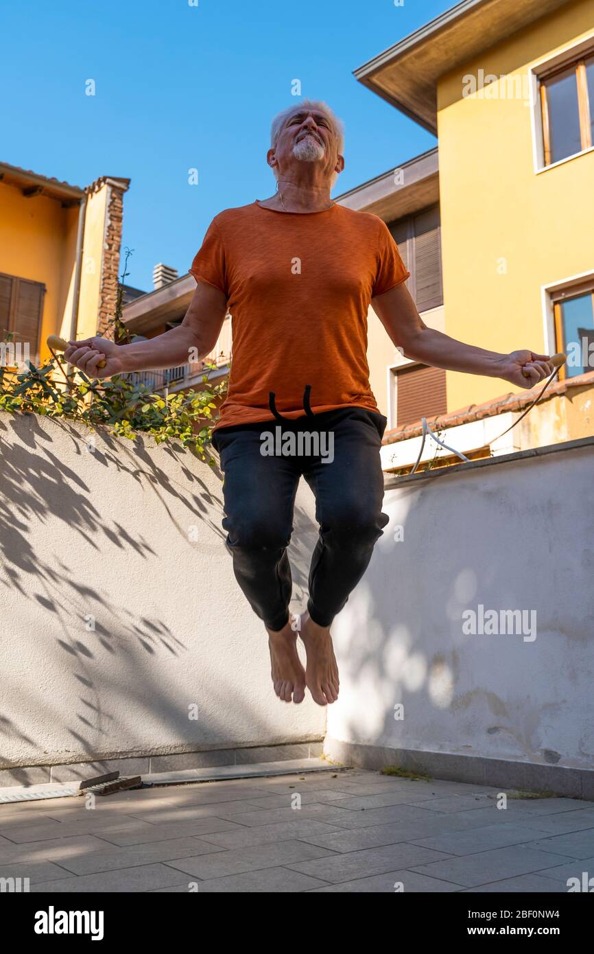 mature man is training by jumping rope on the terrace of his house ...