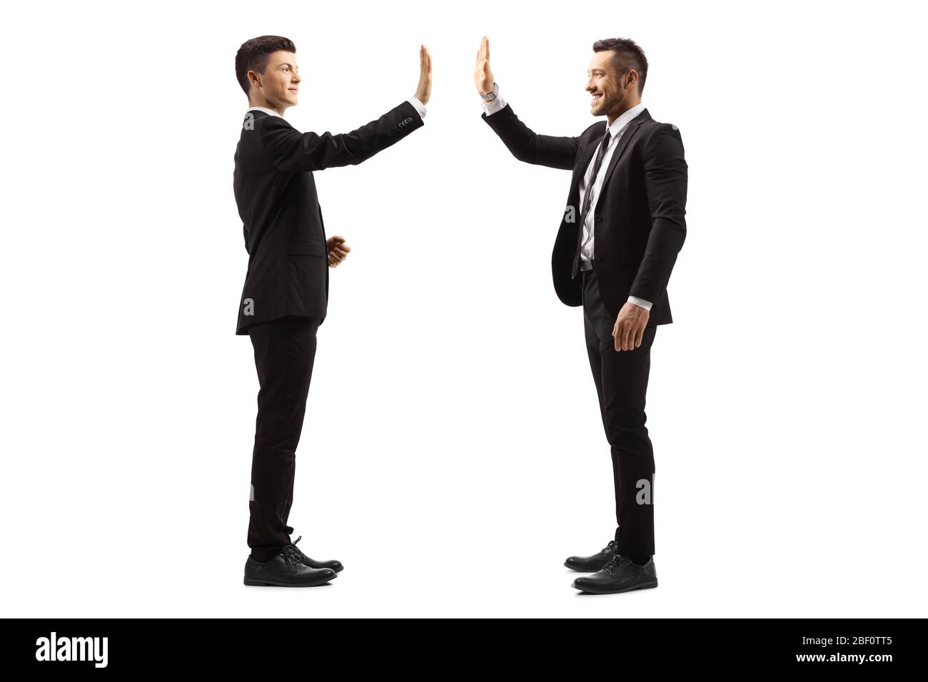 Full length shot of men in suits gesturing high-five isolated on white ...