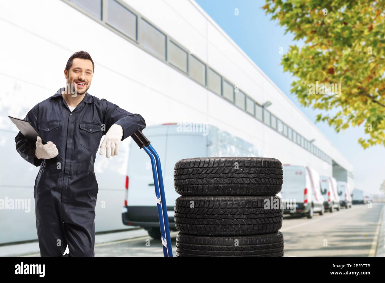 Male worker in a uniform standing with tires on a hand truck outside a ...