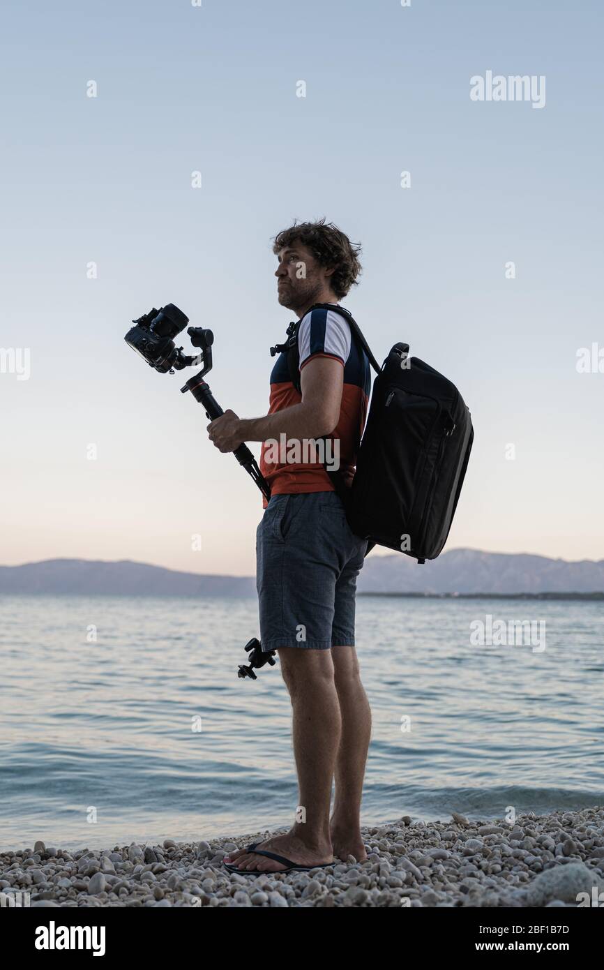 Young male photographer standing on pebble beach in the evening ...
