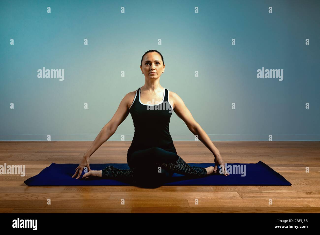 Adult woman 45-55 years old in good shape doing yoga posing on a blue ...
