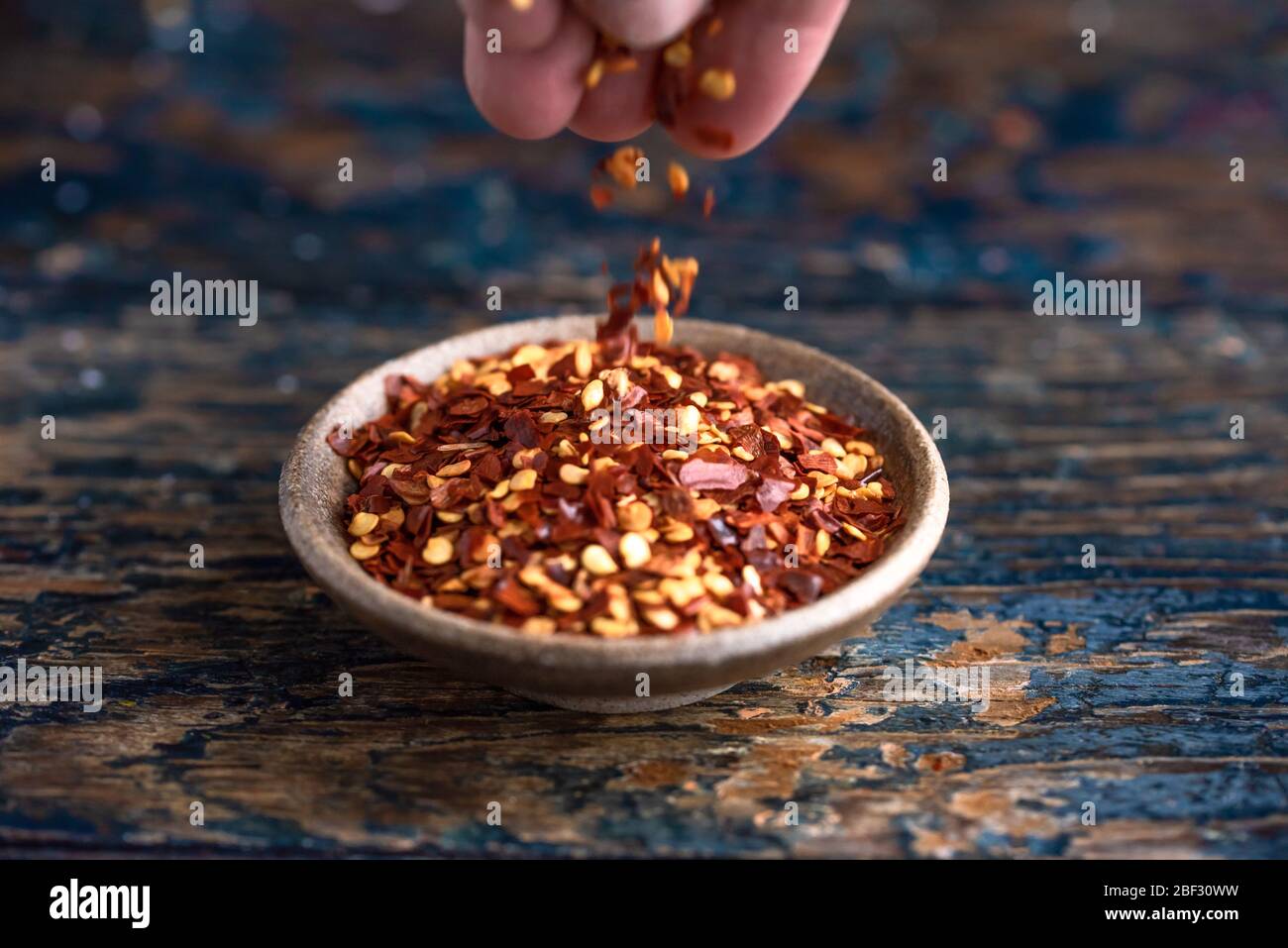 Sprinkling Red Pepper Flakes in a Bowl Stock Photo - Alamy
