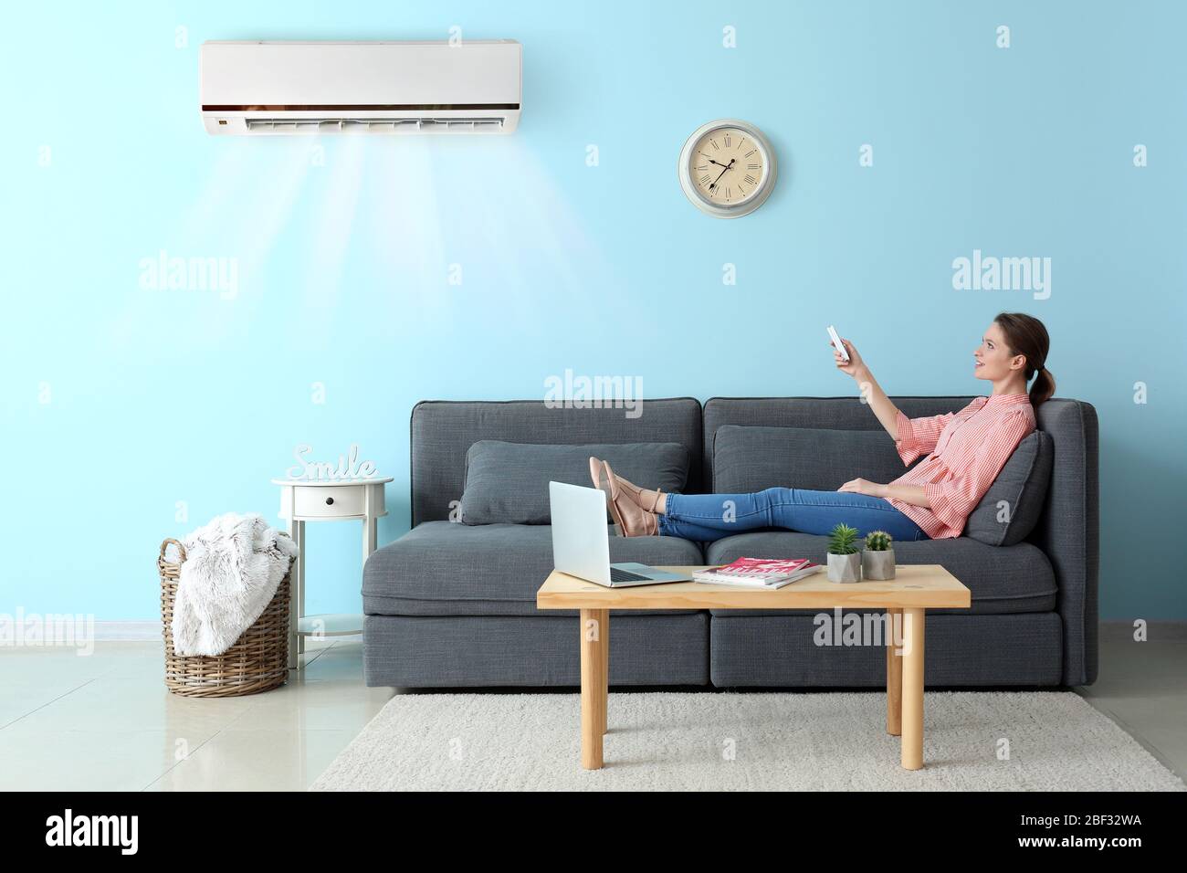Young woman switching on air conditioner at home Stock Photo - Alamy
