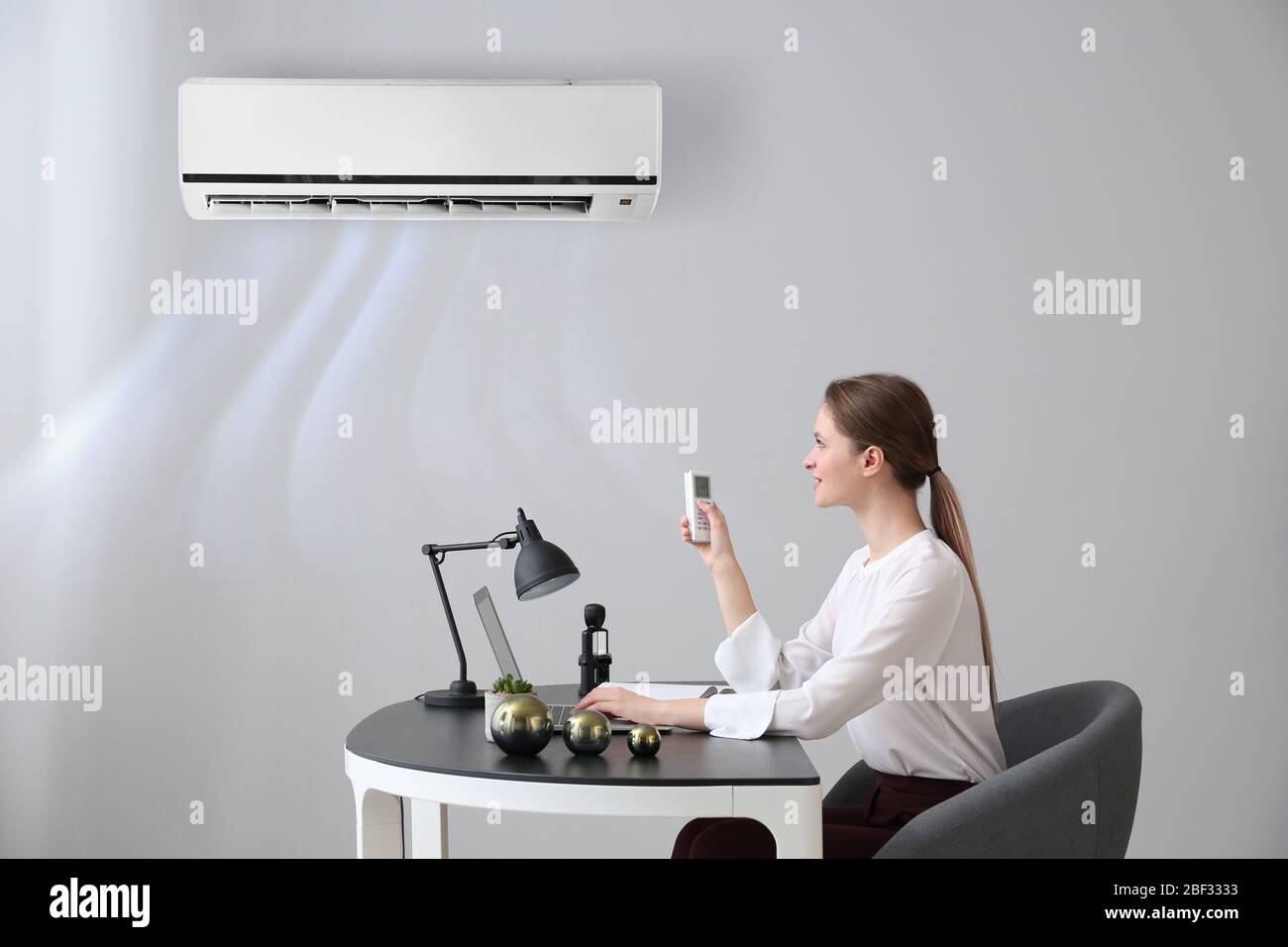 Young woman switching on air conditioner in office Stock Photo - Alamy