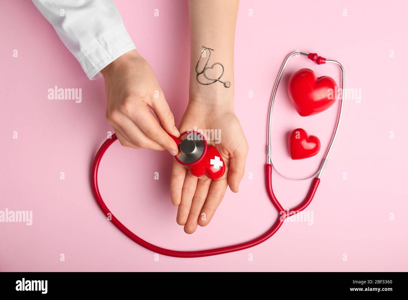 Hands of cardiologist with stethoscope and hearts on color background ...
