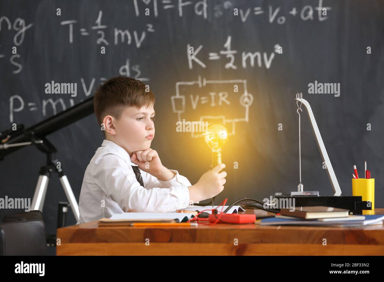 Cute little boy with glowing light bulb at physics lesson in classroom ...