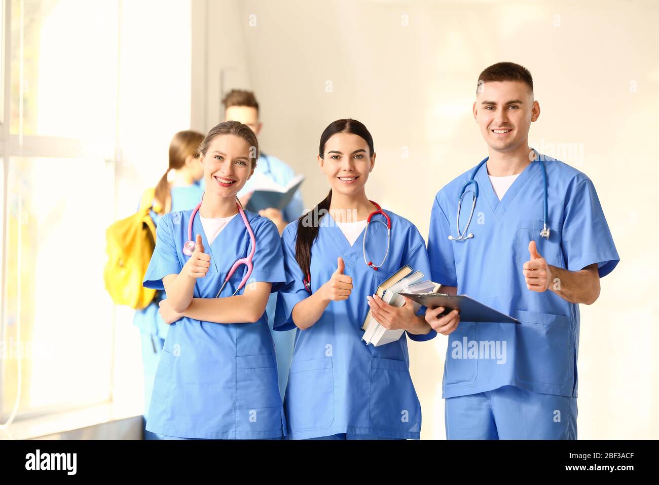 Group of medical students showing thumb-up gesture in hall of clinic ...
