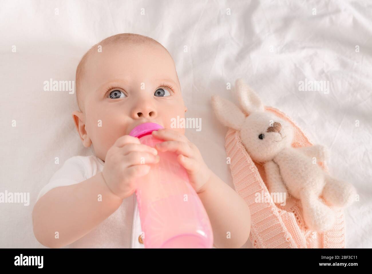 Portrait of cute little baby drinking milk from bottle on bed Stock ...