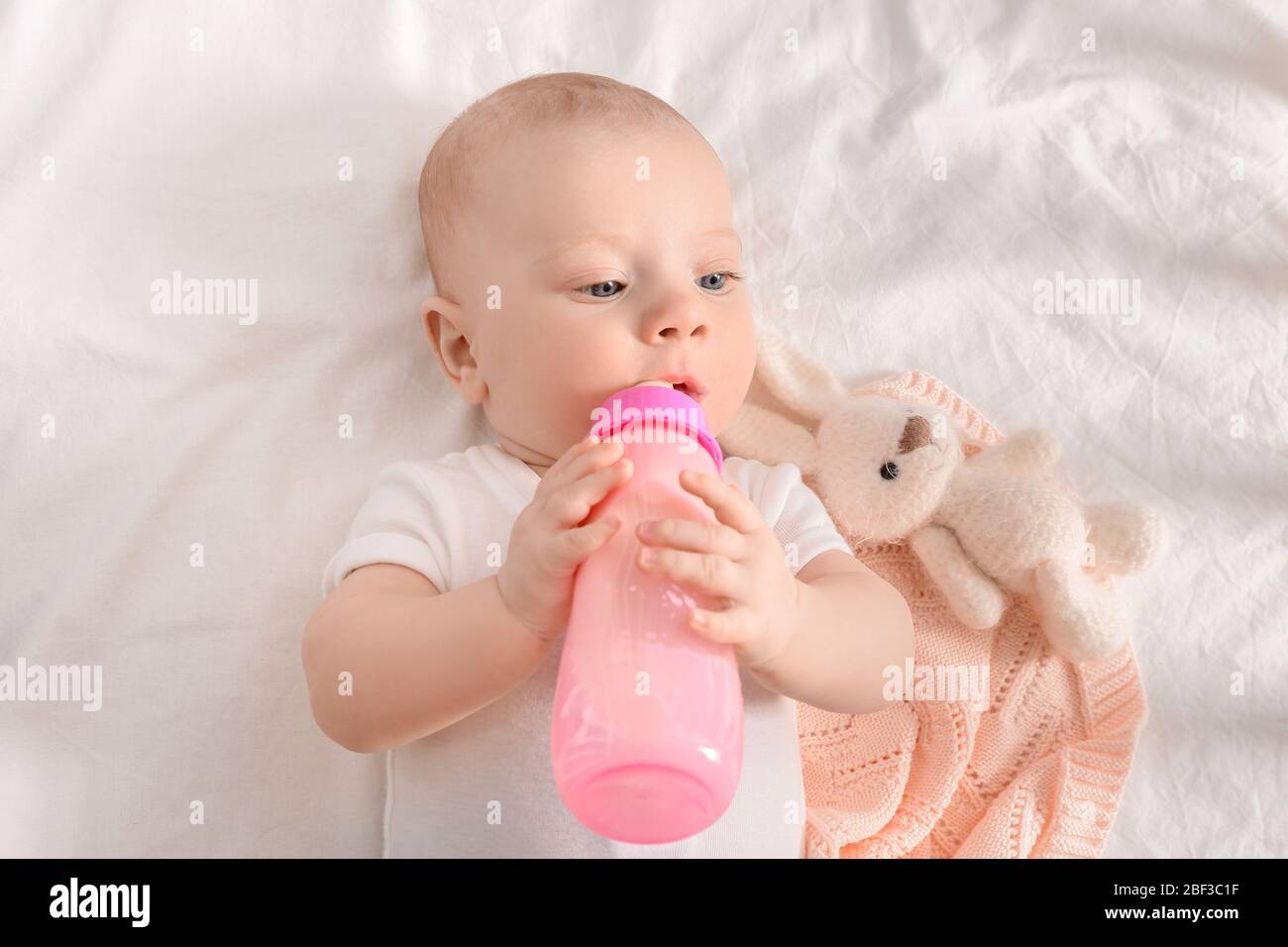 Portrait of cute little baby drinking milk from bottle on bed Stock ...