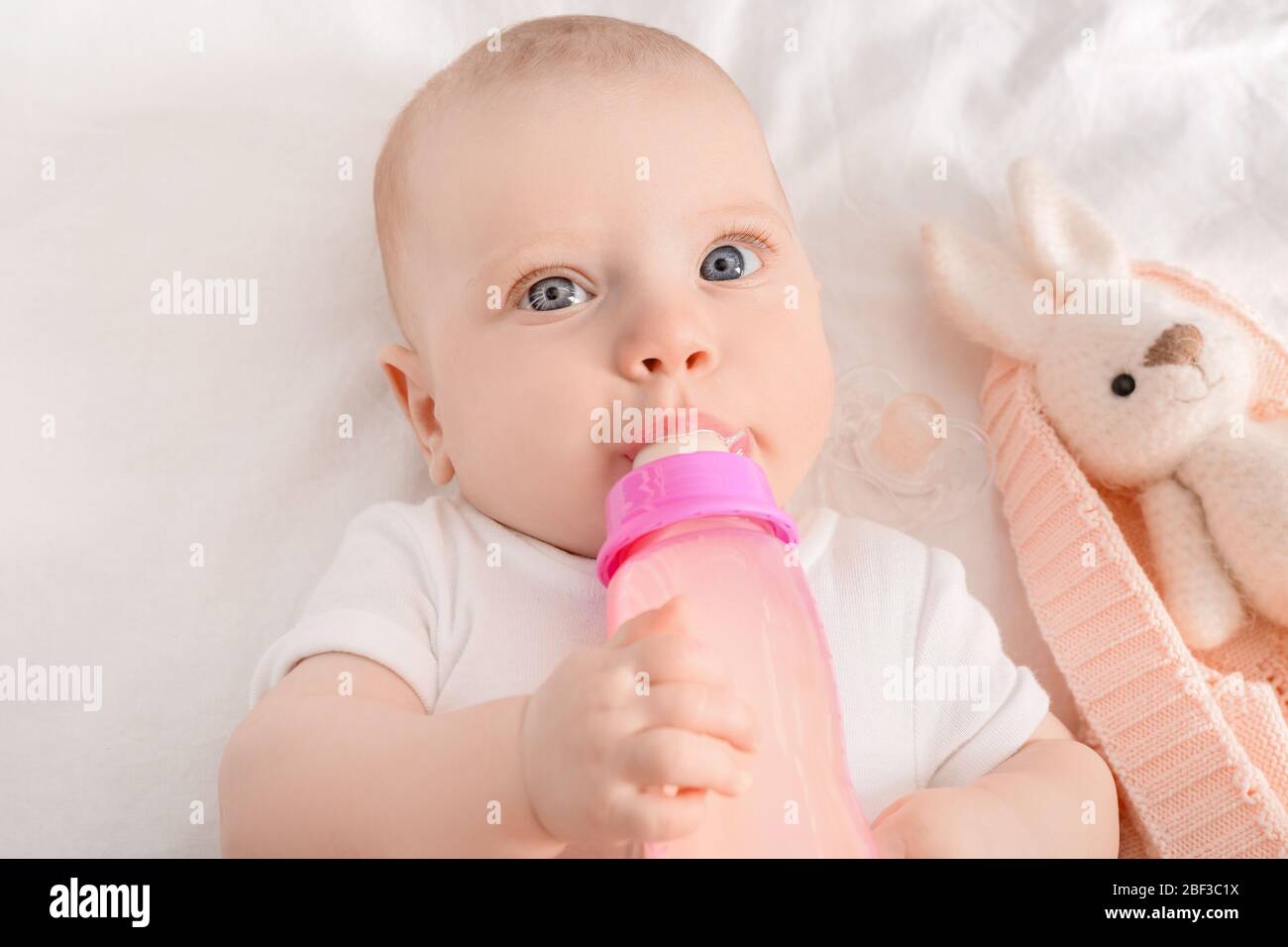 Portrait of cute little baby drinking milk from bottle on bed Stock ...