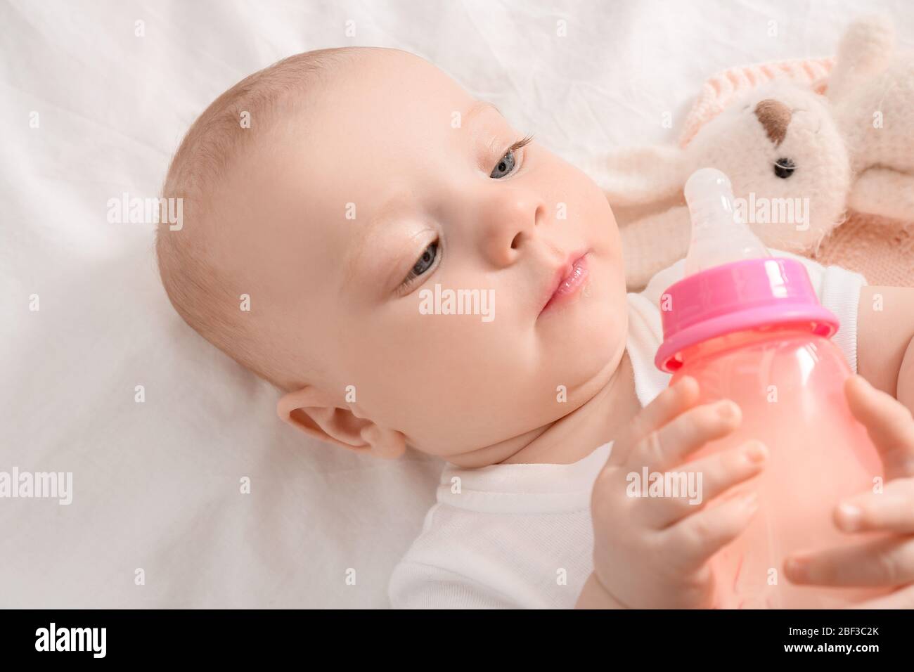 Portrait of cute little baby drinking milk from bottle on bed Stock ...